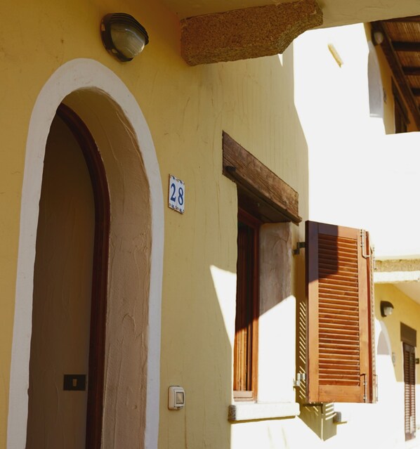 Fachada de um edifício com porta, placa de número e venezianas de madeira.