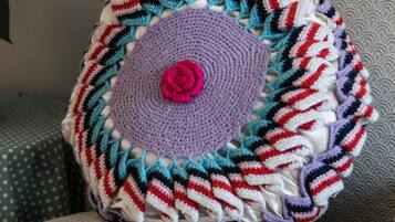 Um travesseiro de crochê com um desenho floral central, colocado sobre uma cadeira com almofada texturizada.