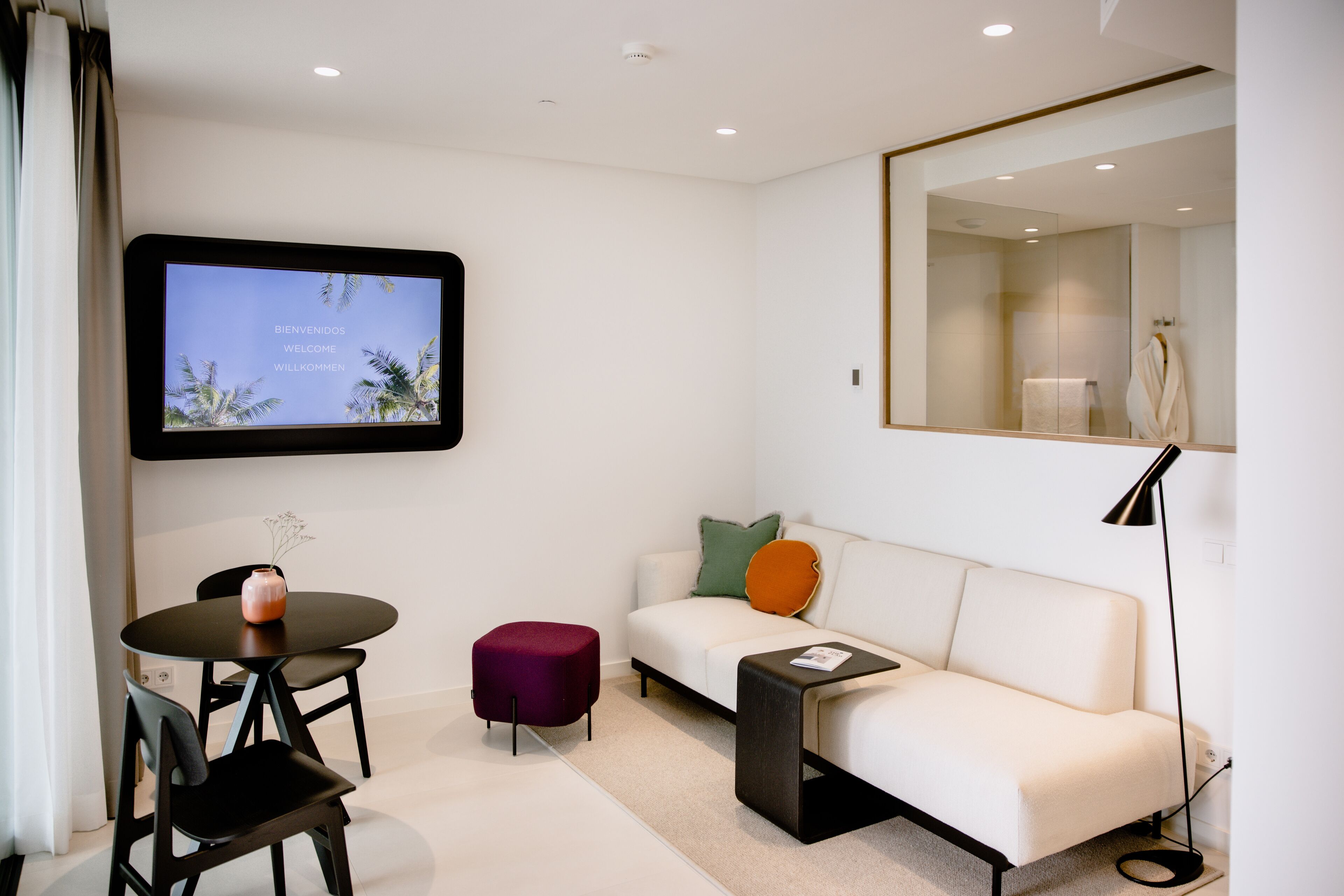 Uma sala de estar moderna com uma TV de tela plana, um sofá, uma mesa de centro e uma pequena mesa redonda com um vaso.