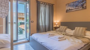 Quarto de hotel com cama, mesa de cabeceira, um quadro e vista pela porta aberta.