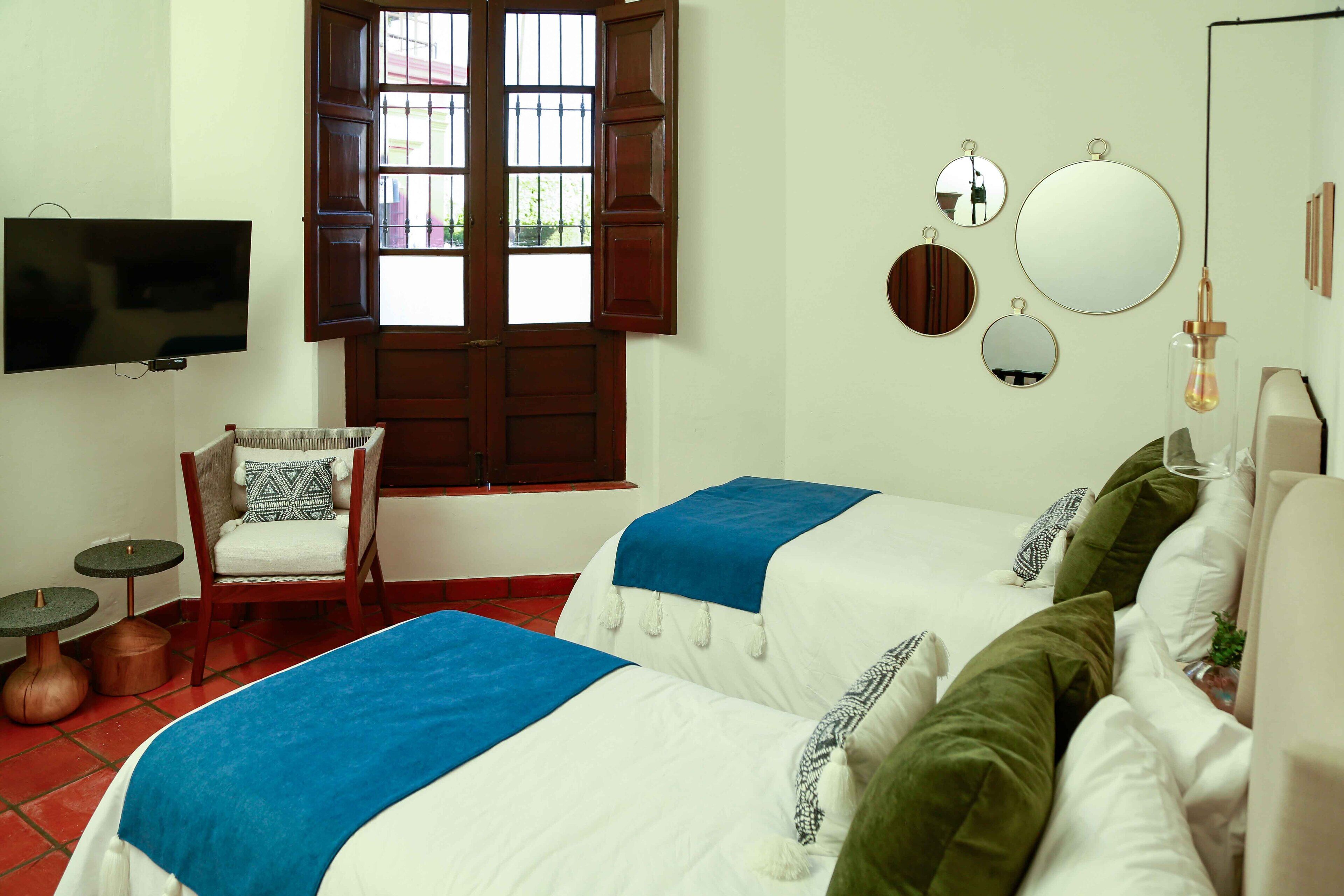 Quarto de hotel com duas camas, televisão, uma cadeira e janela com vista.