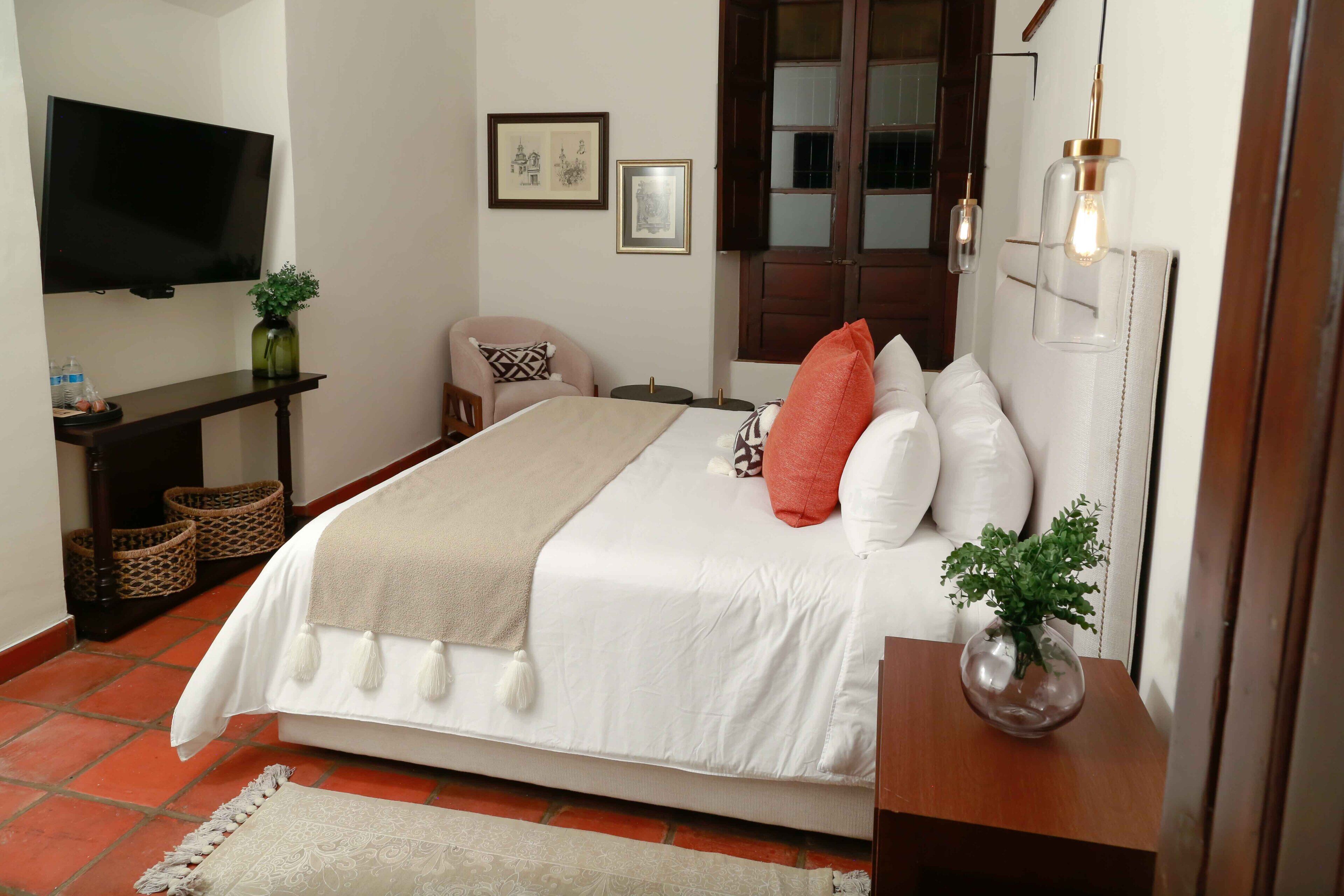 Quarto bem arrumado com cama, mesas de cabeceira, televisão e janela com persianas de madeira.