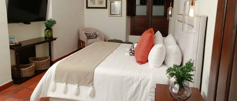 Quarto bem arrumado com cama, mesas de cabeceira, televisão e janela com persianas de madeira.