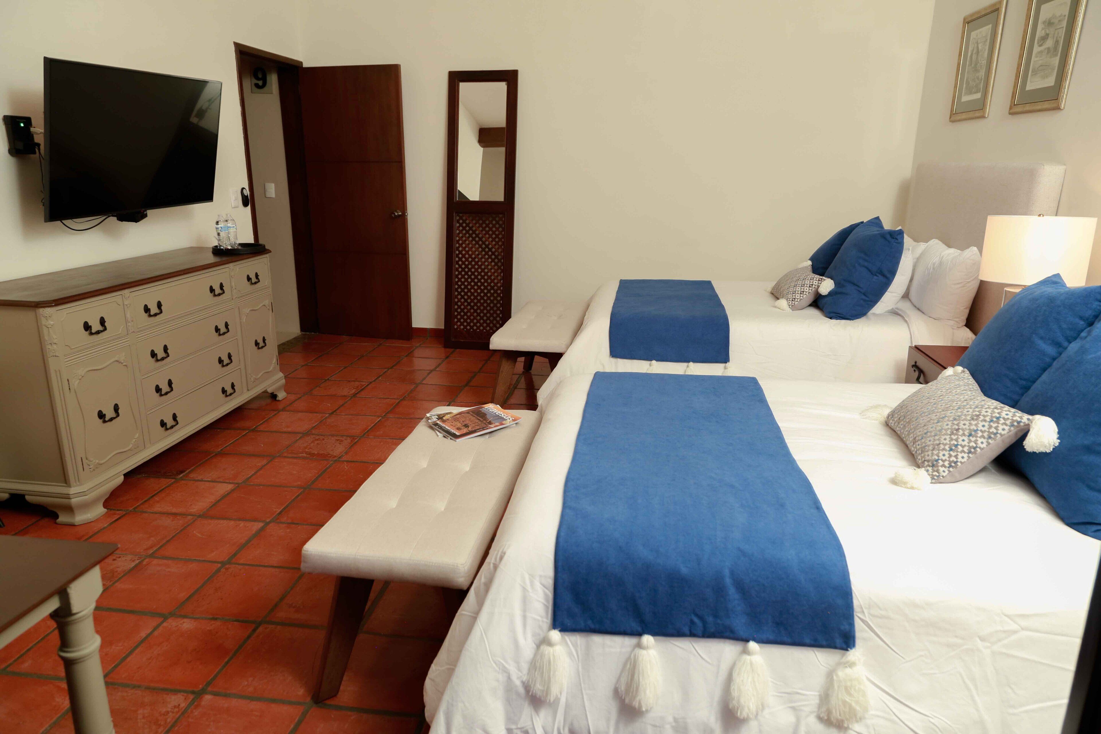 Quarto de hotel com duas camas, uma televisão, um aparador e um banco.