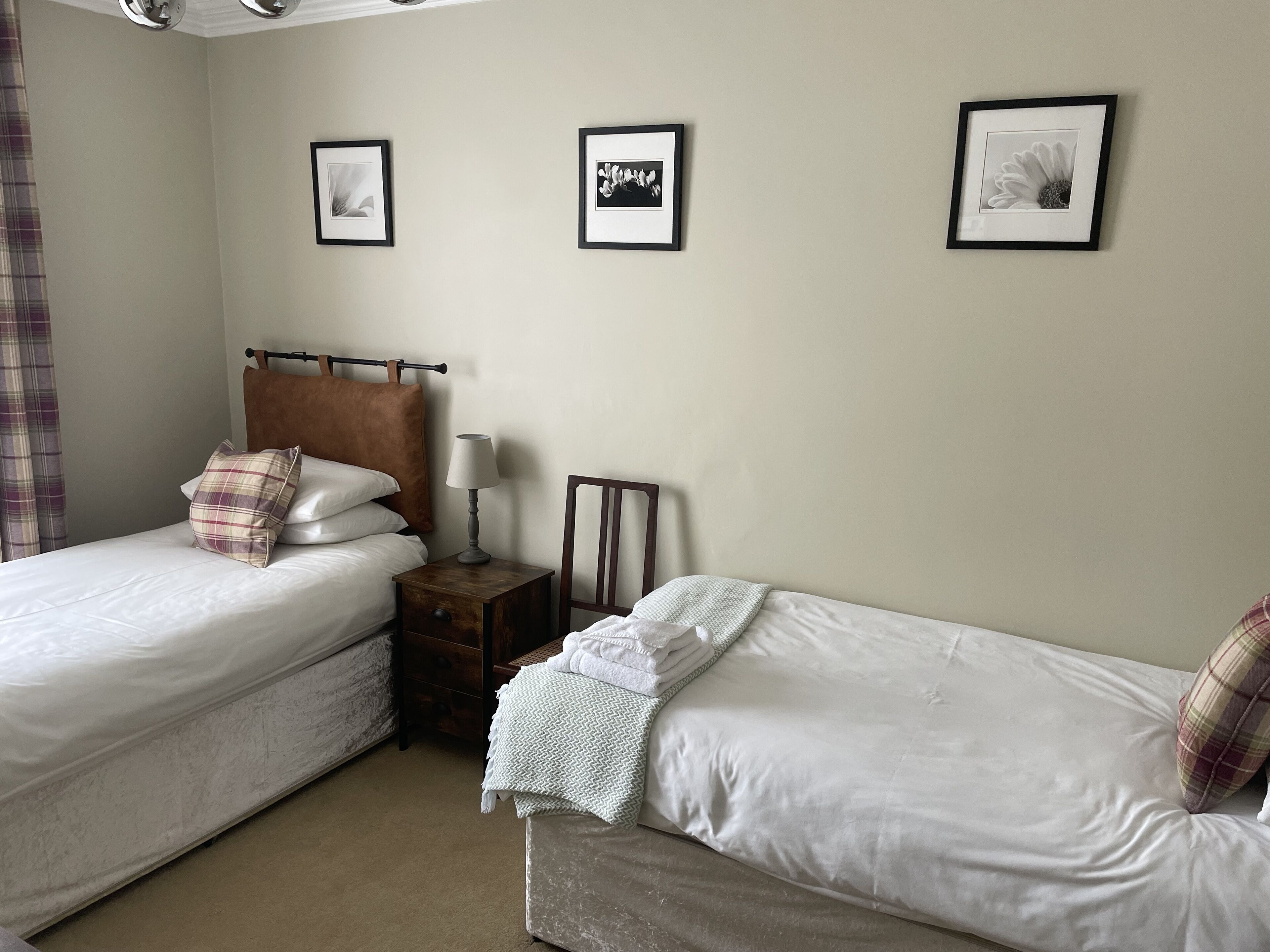 Quarto com duas camas, uma mesinha de cabeceira e três quadros na parede.