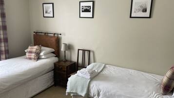 Quarto com duas camas, uma mesinha de cabeceira e três quadros na parede.
