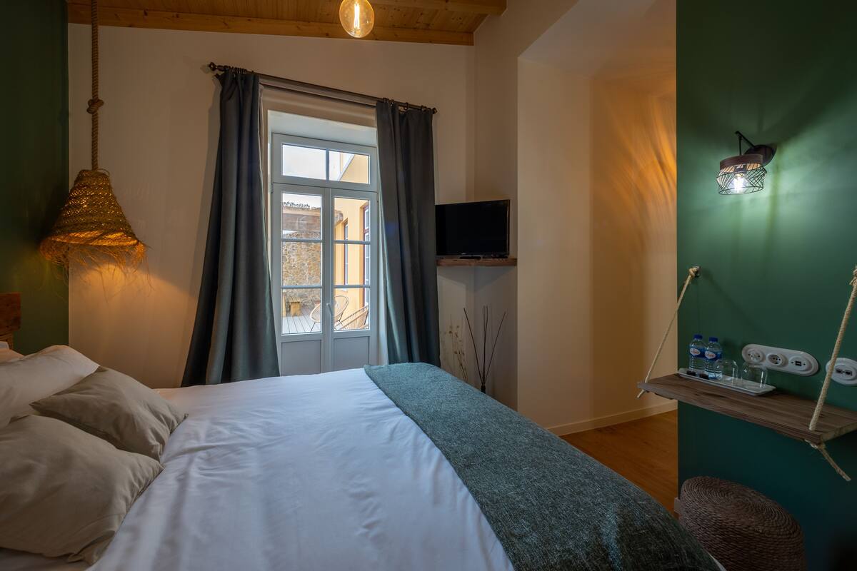 Quarto com cama, luminária pendente, televisão e um pequeno estante com garrafas e copos.