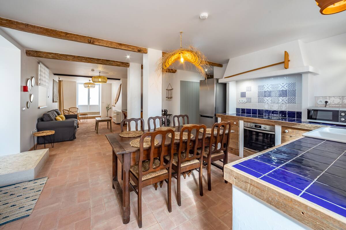 Uma sala de estar ampla com uma mesa de jantar e cadeiras, um sofá e uma cozinha com azulejos azuis na parede.