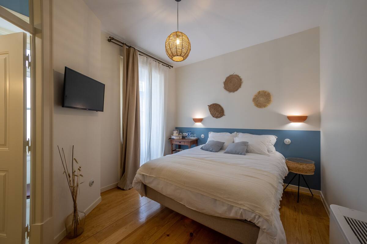 Quarto com cama, televisão, mesa de cabeceira, abajur e arte decorativa na parede.