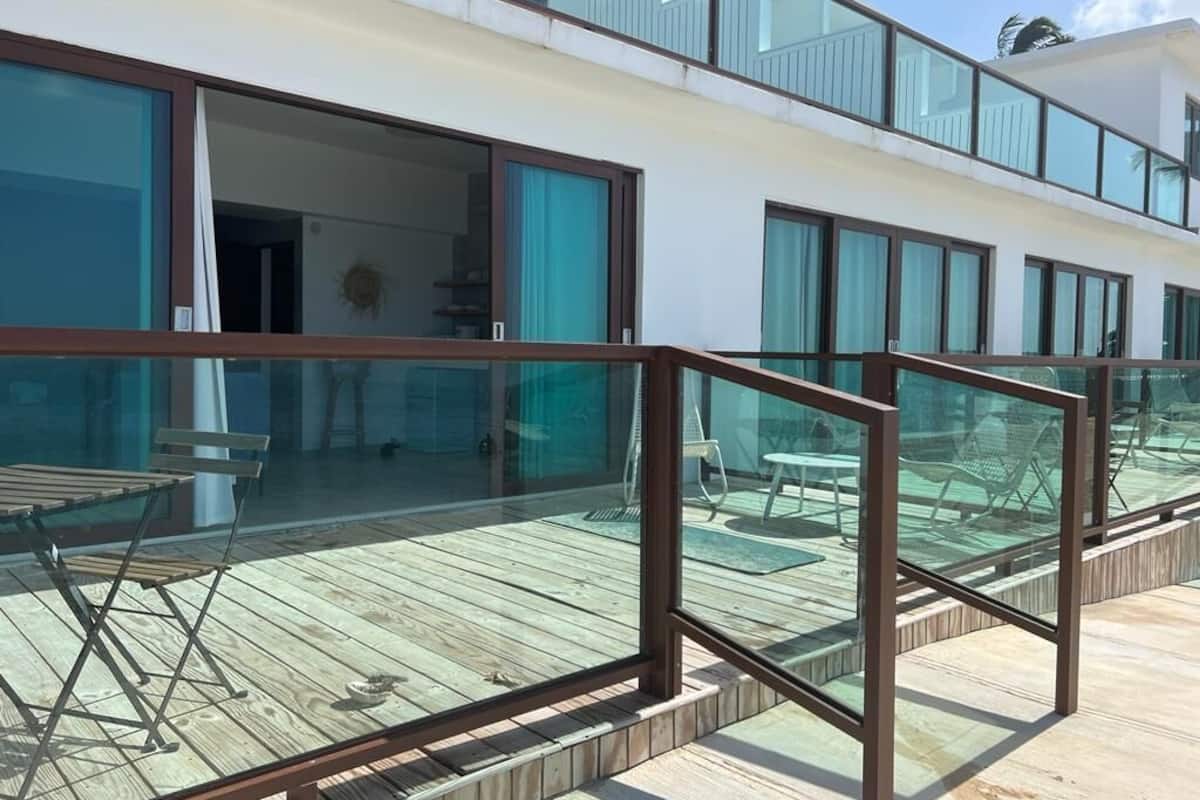 Um edifício moderno de vários andares com um deck de madeira, guarda-corpos de vidro e área de estar externa.