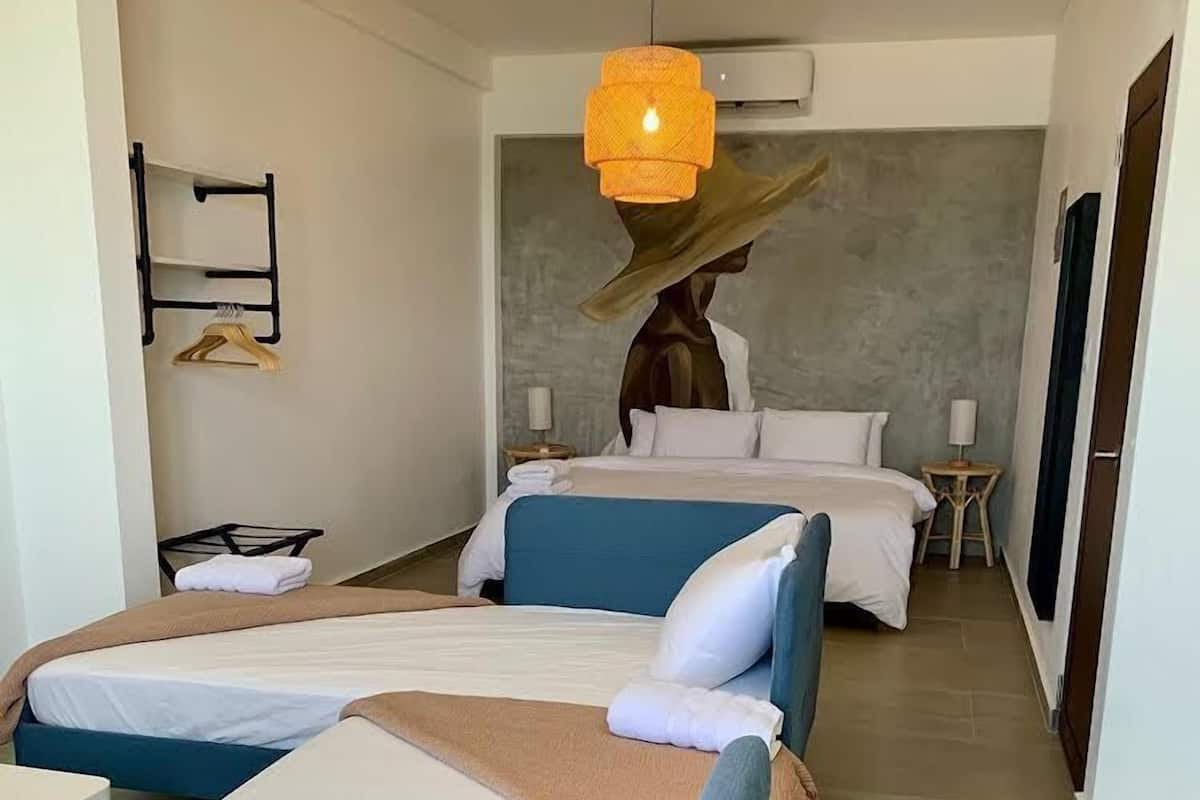 Quarto de hotel com duas camas, luminária pendente e uma grande pintura abstrata na parede.