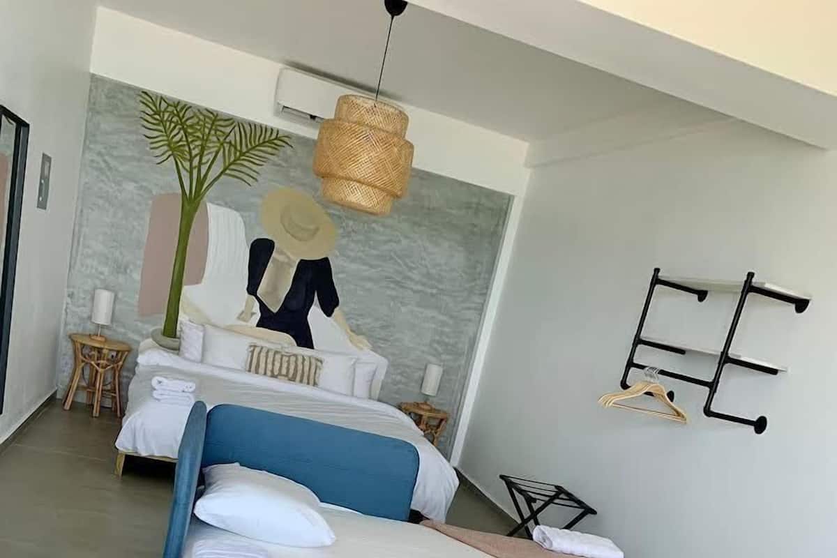 Quarto de hotel moderno com uma cama grande, um sofá-cama menor, uma pequena mesa e um lustre.