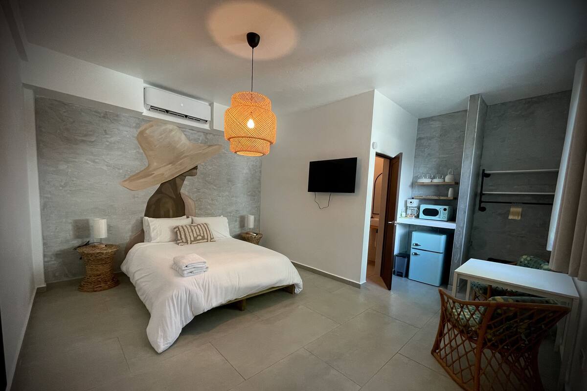 Quarto moderno com cama, luminárias de cabeceira, televisão e uma kitchenette.