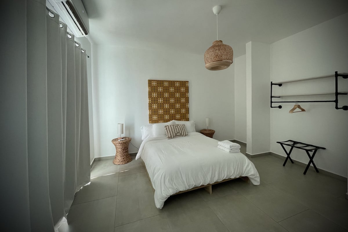 Quarto moderno com cama, mesas de cabeceira, luminária pendente e prateleira na parede.