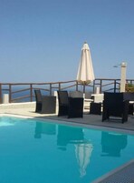 Área de piscina com espreguiçadeiras e um guarda-sol, com vista para um céu claro.