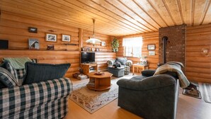 Interior acolhedor de uma cabana com um sofá quadriculado, uma poltrona cinza, mesa de centro de madeira, televisão e lareira de tijolos.