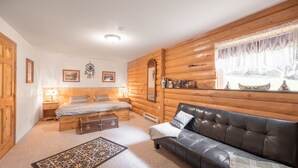 Um quarto acolhedor em cabana de madeira, com uma cama, um sofá de couro, um tapete estampado e uma janela com cortinas de renda.