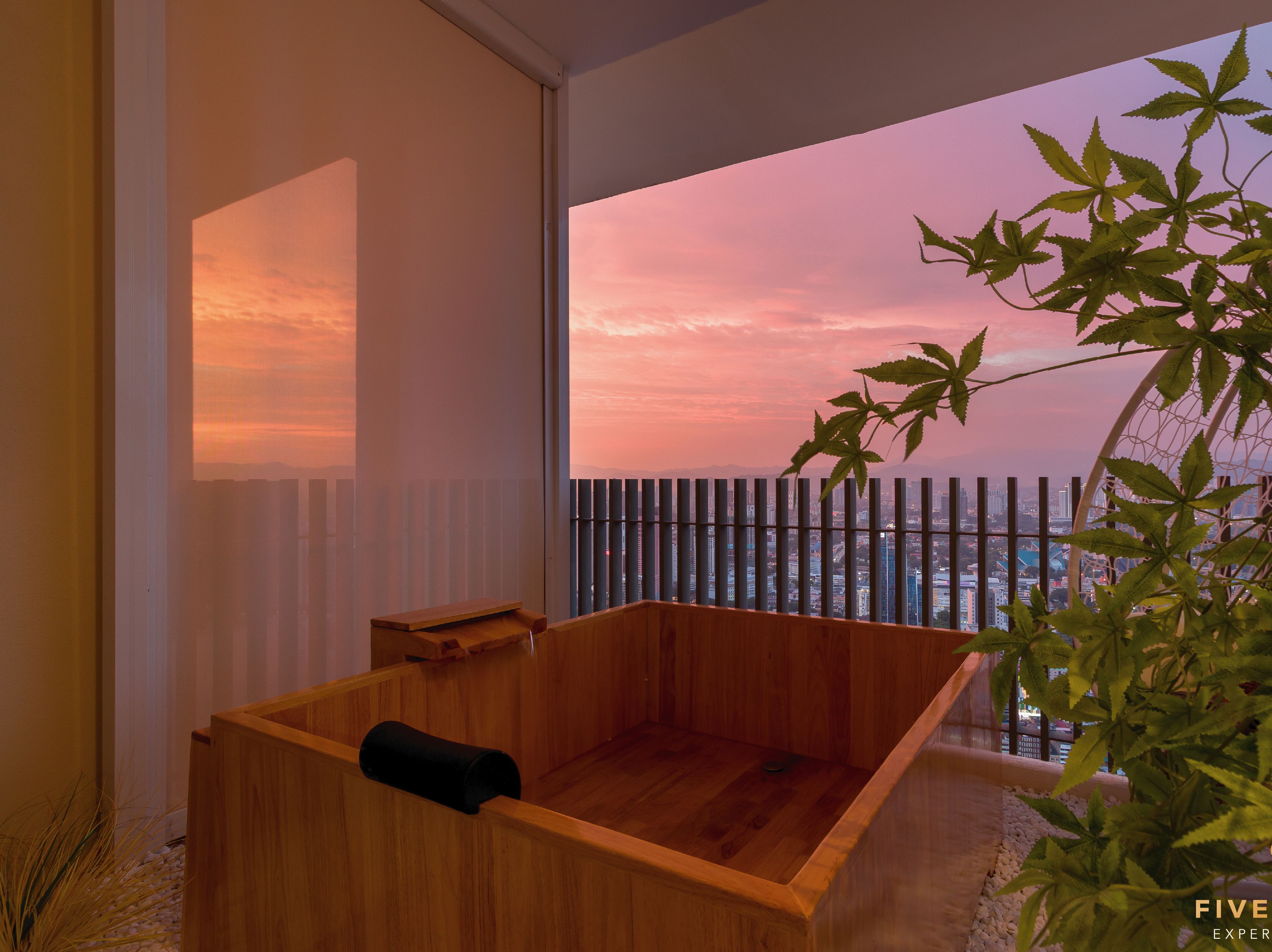 Uma banheira de madeira em um quarto com uma grande janela com vista para a paisagem urbana ao pôr do sol.