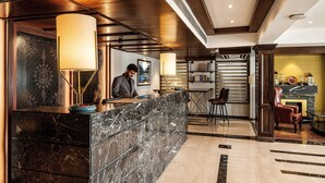 Um hall de hotel com uma recepção de mármore, lareira e área de estar com poltronas de couro.
