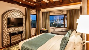 Quarto de hotel com uma cama grande, uma televisão de tela plana na parede decorativa, vista para a cidade pela janela e um ventilador de teto.