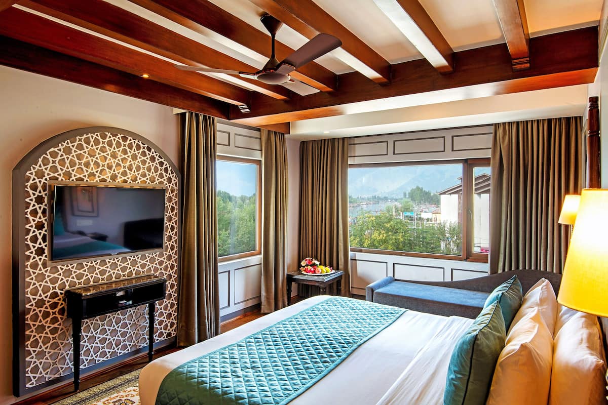 Quarto de hotel com uma cama grande, televisão fixada numa parede decorativa, ventoinha no teto e janela com vista para a cidade.