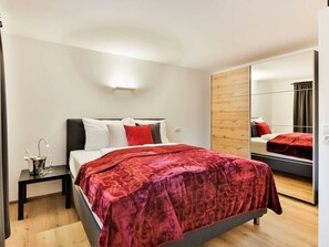 Quarto de hotel moderno com uma cama grande, uma mesinha de cabeceira com garrafa e copos, painel de parede de madeira e um espelho refletindo o quarto.