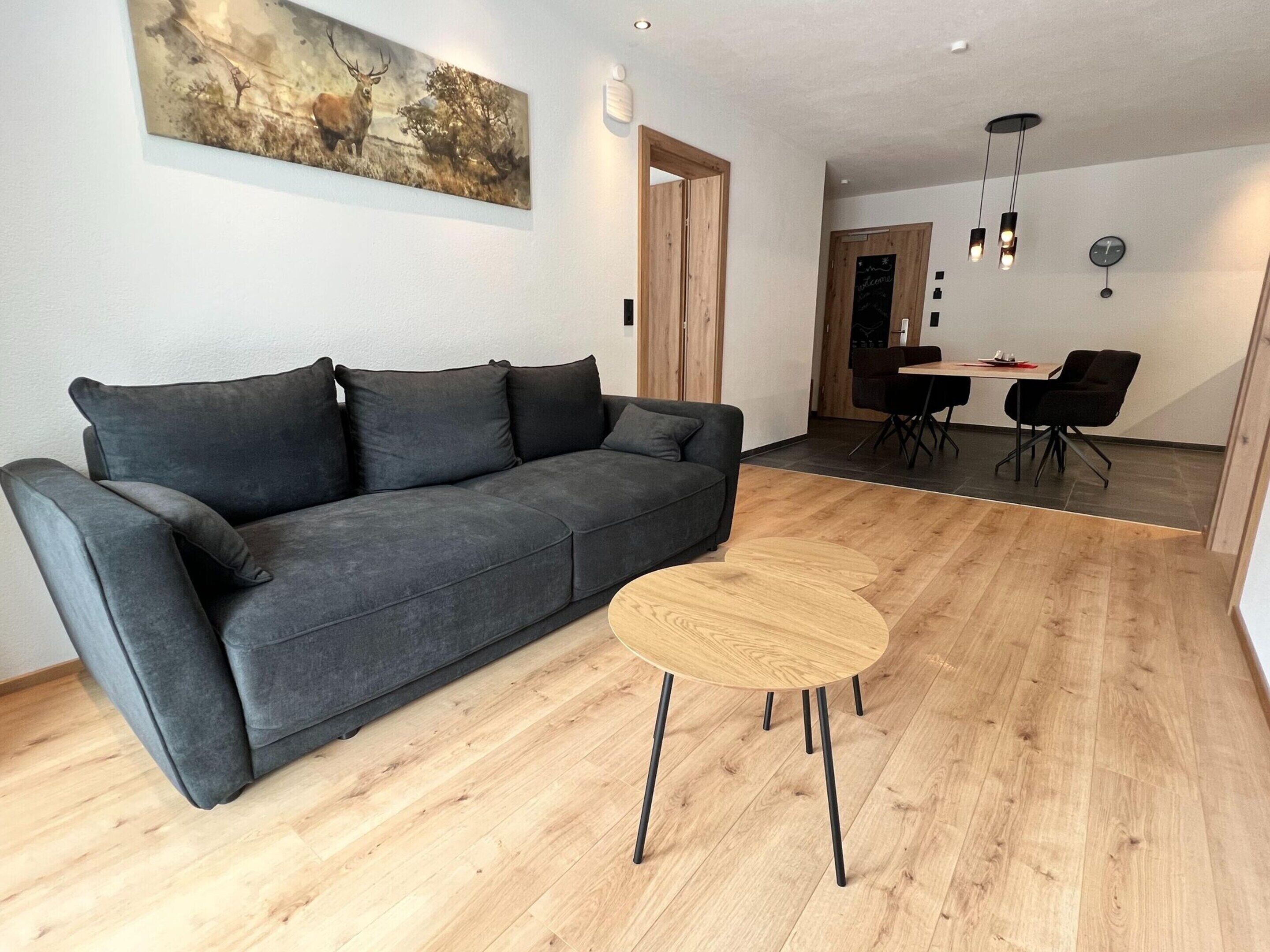 Uma sala de estar moderna com um sofá cinzento, uma mesa de centro de madeira e um espaço de refeições com uma mesa e cadeiras.