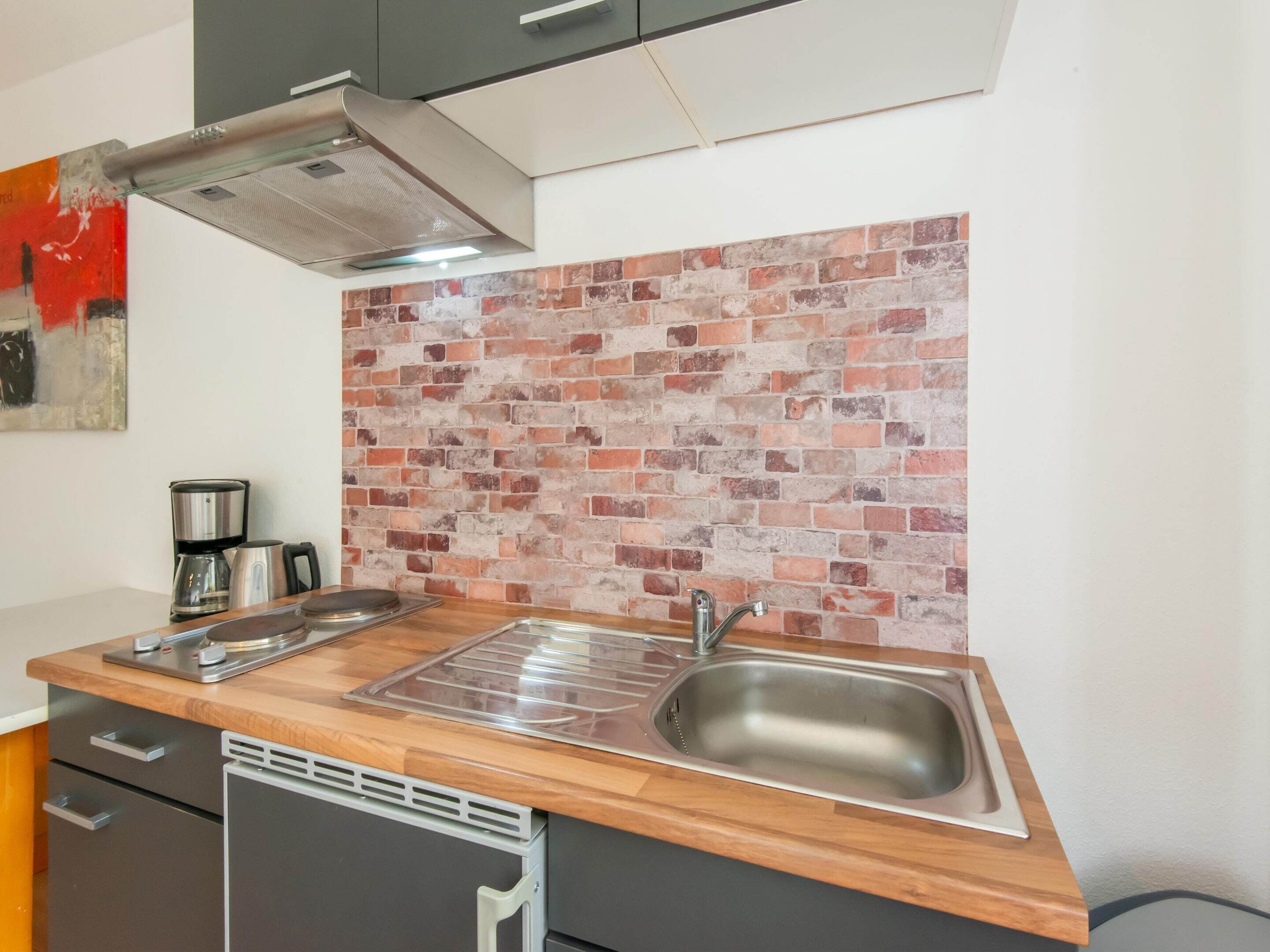 Cozinha moderna com painel de tijolos, pia de aço inoxidável e cafeteira.