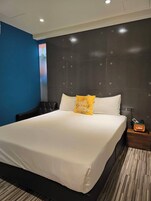 Quarto de hotel moderno com uma cama grande, uma mesinha de cabeceira com rádio e uma parede azul de destaque.