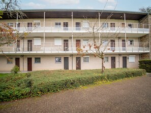 Um edifício de vários andares com telhado plano, varandas e um acesso pavimentado.