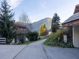 Uma rua rural com casas, uma montanha ao fundo e céu claro.