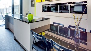 Uma cozinha moderna com ilha central, fornos embutidos e área de jantar com mesa e cadeiras de vidro.
