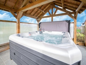 Uma banheira de hidromassagem sob uma pérgola de madeira, com vista para o céu e uma casa ao fundo.