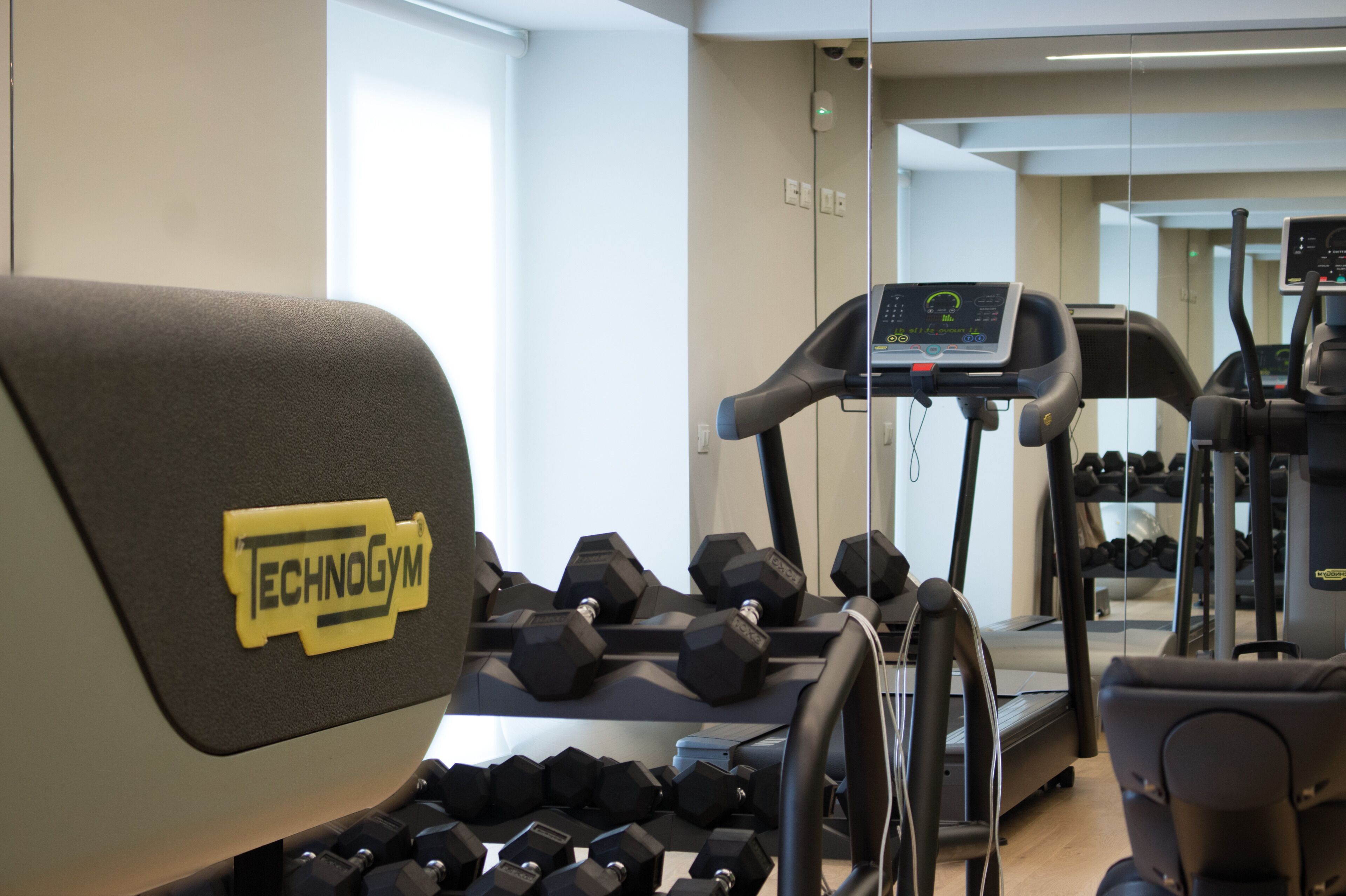 Academia com equipamentos de ginástica, incluindo halteres, esteira e bicicleta ergométrica.