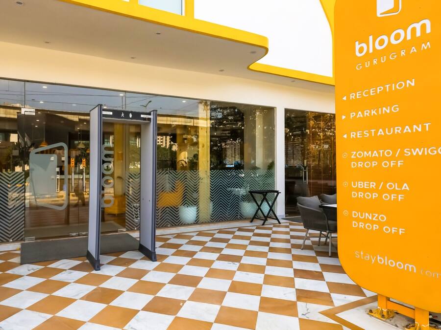 Um saguão de hotel com piso xadrez, portas de vidro e um balcão de recepção.