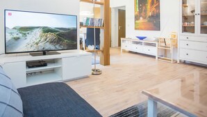 Uma sala de estar moderna com televisão de tela plana, estantes de madeira, um armário branco e um quadro grande na parede.