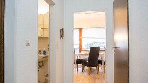 Um corredor leva a uma área de refeições com mesa e cadeiras, uma janela com vista e uma cozinha com armários e pia.