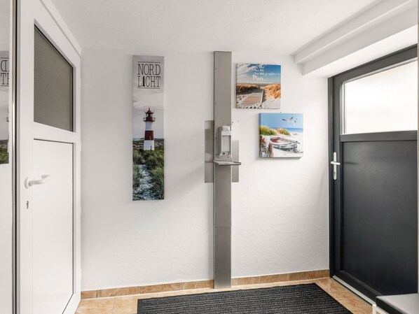 Um corredor com uma porta branca, uma porta preta e três quadros na parede.