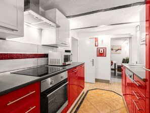 Uma cozinha moderna com armários vermelhos, bancada preta e eletrodomésticos de aço inoxidável.