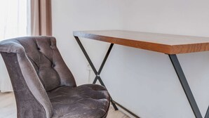 Canto de um quarto com uma poltrona de veludo escuro e uma mesa de madeira com pés de metal.