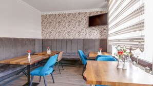 Um restaurante com mesas de madeira e cadeiras azuis, um muro decorado com flores e uma televisão montada acima da área de estar.