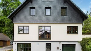 Uma casa de dois andares com telhado inclinado, várias janelas e uma porta de garagem.
