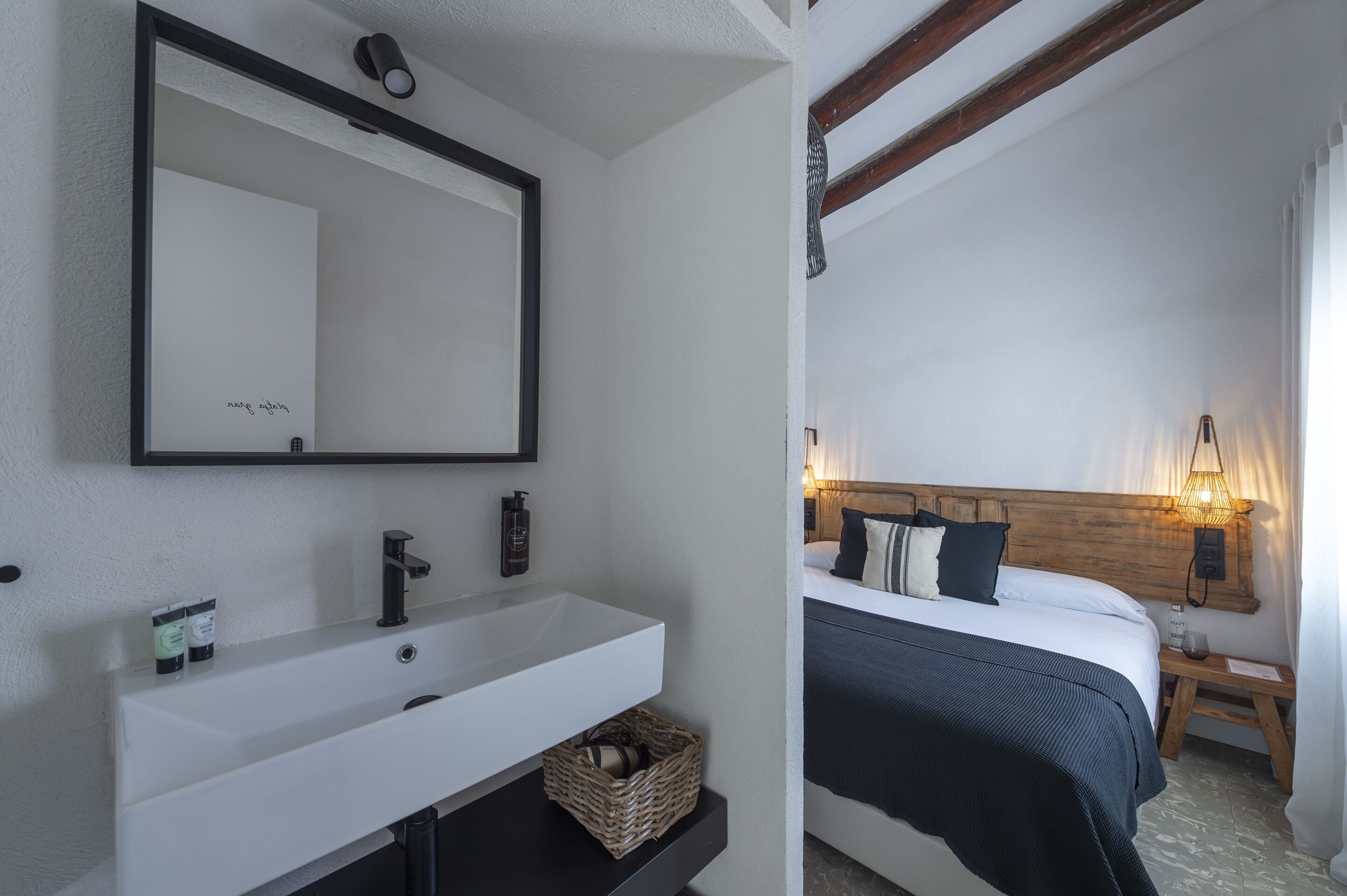 Uma casa de banho moderna com um espelho grande, lavatório branco e uma cabeceira de madeira no quarto adjacente.