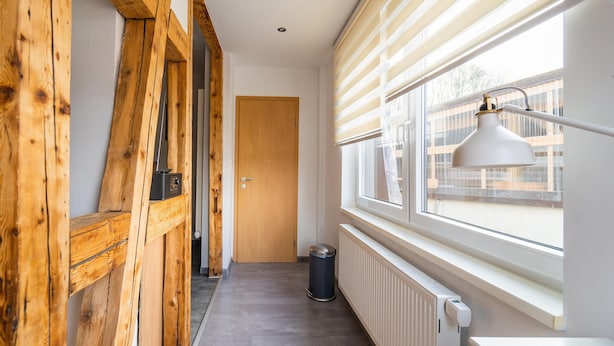 Um corredor com vigas de madeira, um radiador, uma lixeira e uma janela com persianas.