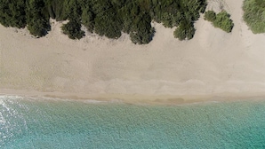 Vista aérea de uma praia com águas turquesa cristalinas e uma costa arenosa.