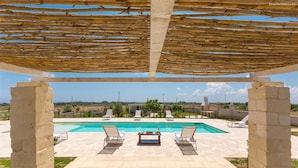 Uma área de piscina com piso de pedra, espreguiçadeiras e uma pérgula.
