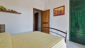Um quarto com uma cama, uma porta de madeira, um guarda-roupa verde e um quadro na parede.