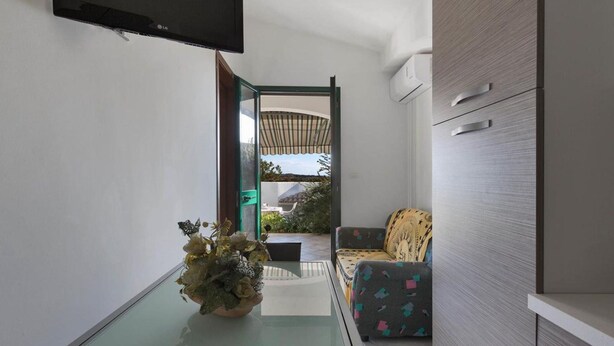 Uma sala de estar moderna com uma mesa de vidro, um sofá com almofada colorida e uma TV fixada na parede.