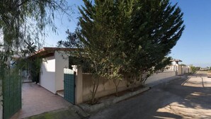 Uma rua residencial com uma casa branca, um portão verde e calçada arborizada.