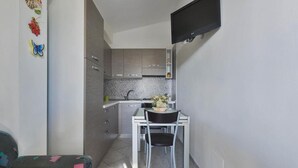 Uma cozinha compacta com uma mesa de jantar e cadeiras, uma TV de tela plana na parede e um revestimento de azulejos.